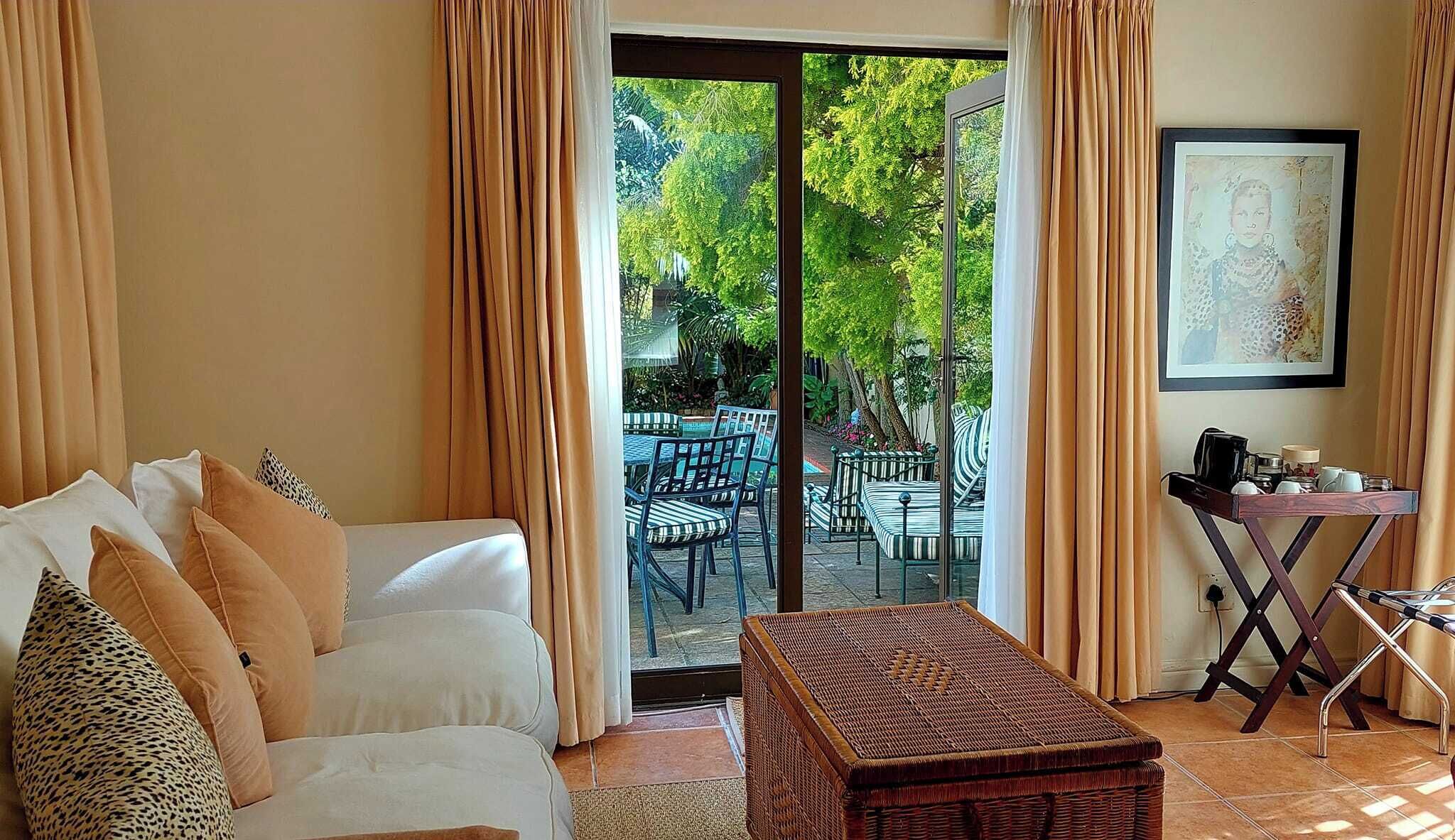 Quarto com sofá, um banquinho de vime, área de refeições com cadeiras e uma mesa, e uma obra de arte emoldurada na parede.