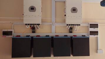 Um painel de controle com dois dispositivos Deye, uma régua de tomadas e três armários pretos.