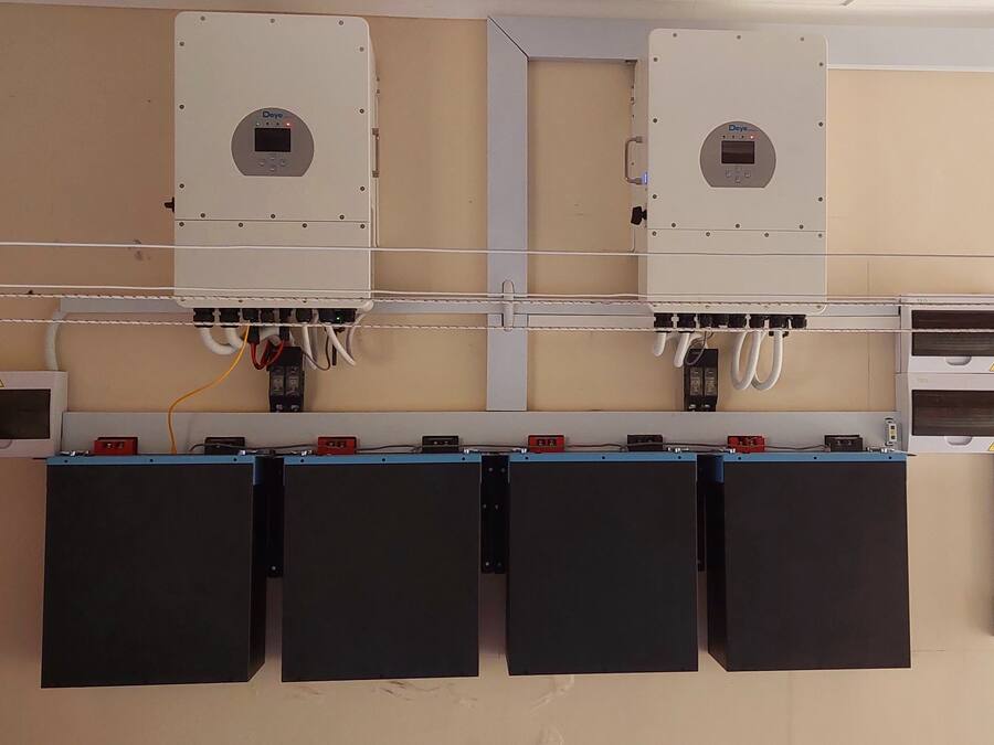 Um painel de controle com dois dispositivos Deye, uma régua de tomadas e três armários pretos.