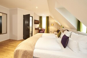 Quarto com cama grande, escrivaninha, cadeira, televisão e janela com cortinas.