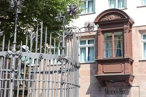 Entrada de hotel com portão de ferro forjado e toldo marrom sobre a porta.