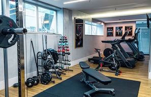 Uma academia com equipamentos de musculação, um banco e máquinas de cardio.
