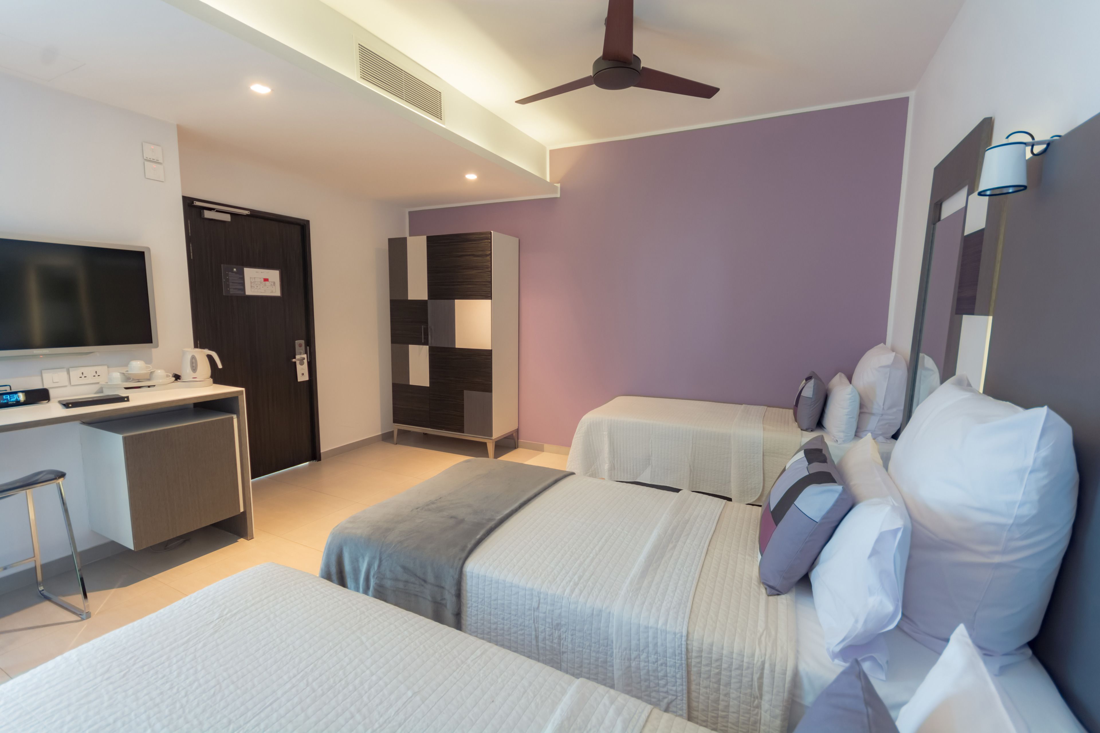 Quarto de hotel com duas camas, uma escrivaninha, televisão e guarda-roupa.