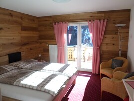 Quarto com painéis de madeira, com uma cama, uma cadeira, um radiador e uma janela com cortinas.