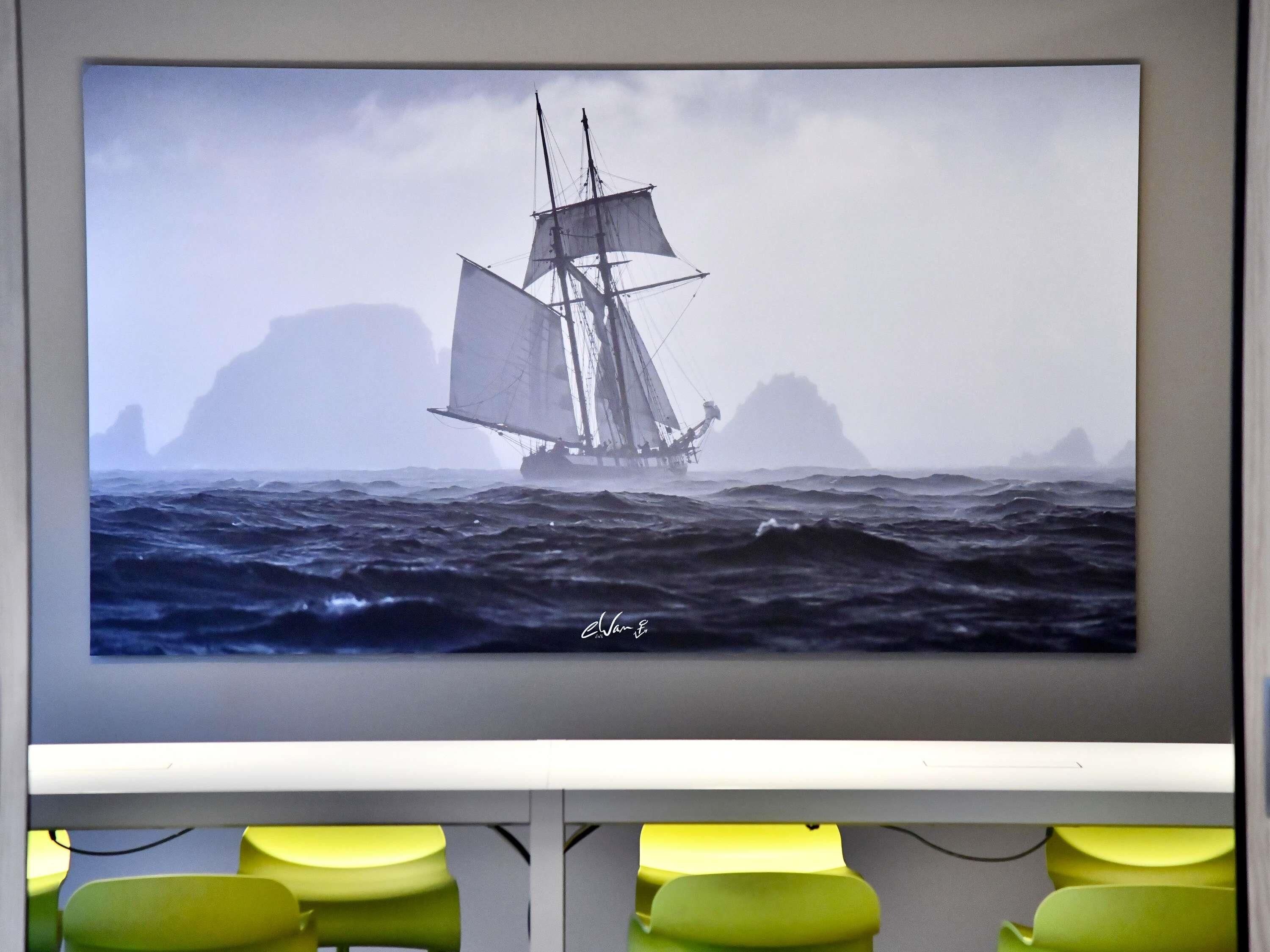 Tela de televisão exibindo um veleiro em mares agitados, com paisagens distantes.