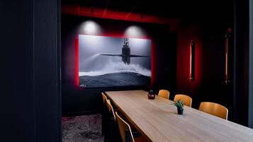 Sala de conferência com uma grande tela fixada na parede exibindo um submarino, uma mesa de madeira e quatro cadeiras.