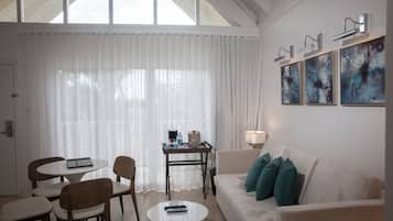 Uma sala de estar moderna com sofá branco, almofadas verde-turquesa, uma mesa de centro redonda e uma área de jantar com cadeiras e uma mesinha.