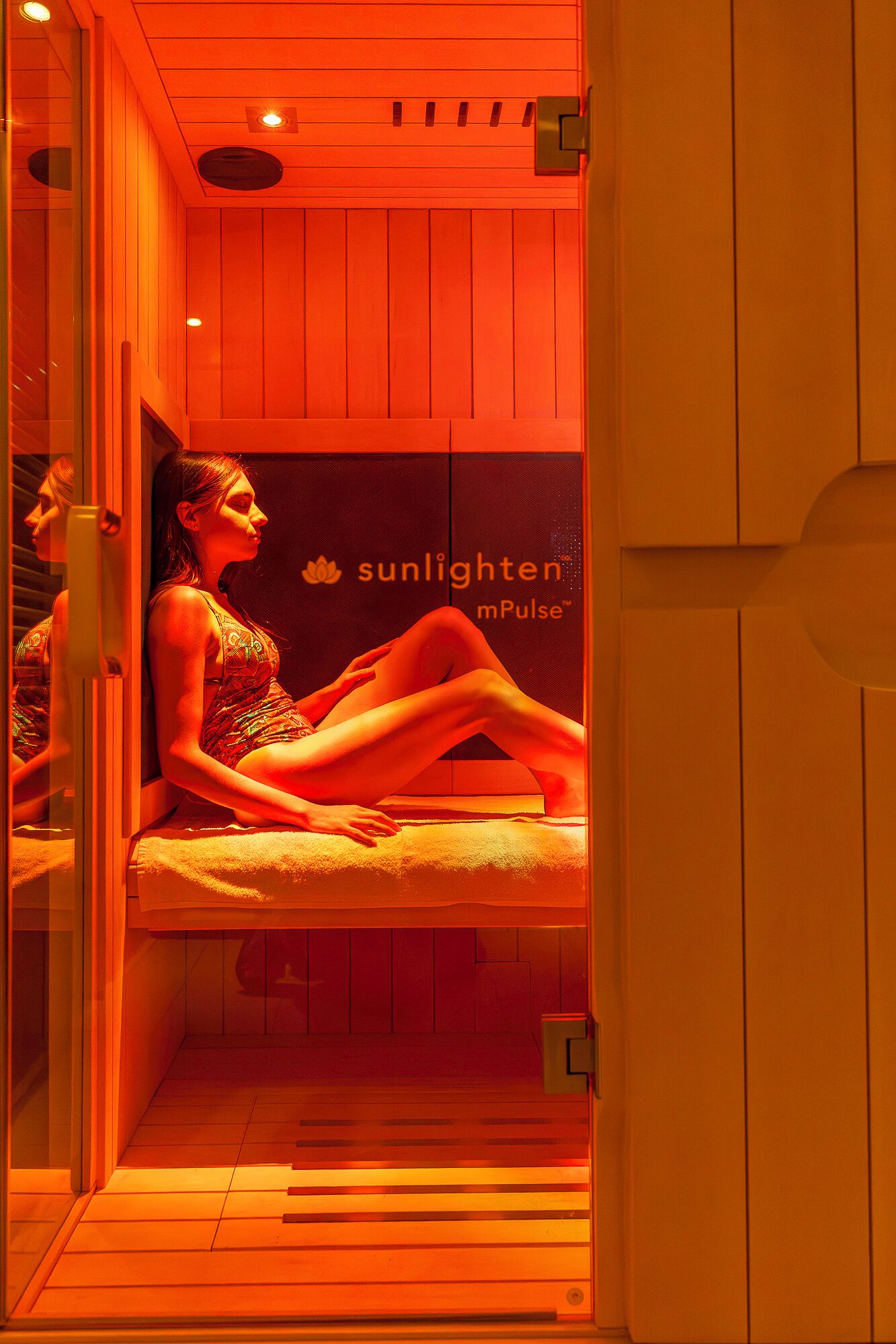 Uma sauna com uma mulher sentada no interior, um logotipo na parede e painéis de madeira.