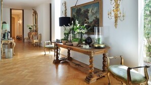 Um quarto com piso de madeira, uma pintura grande na parede, uma mesa com um vaso de flores e uma cadeira.