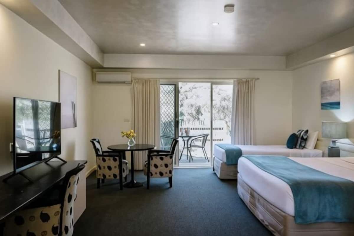 Quarto de hotel com uma cama, uma mesa com televisão, uma mesa de jantar com cadeiras e uma varanda com vista.