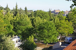 Um camping com veículos recreativos e tendas, cercado por árvores densas e uma vista distante de edifícios.