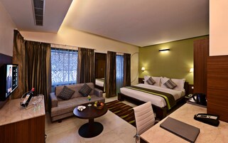 Quarto de hotel com cama, sofá, escrivaninha e televisão.