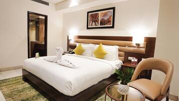 Quarto de hotel com uma cama, uma cadeira, uma mesinha com uma planta e um quadro na parede.