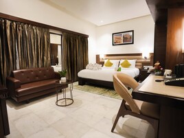 Quarto de hotel com uma cama, um sofá de couro marrom, uma mesa redonda pequena, uma escrivaninha e uma cadeira.