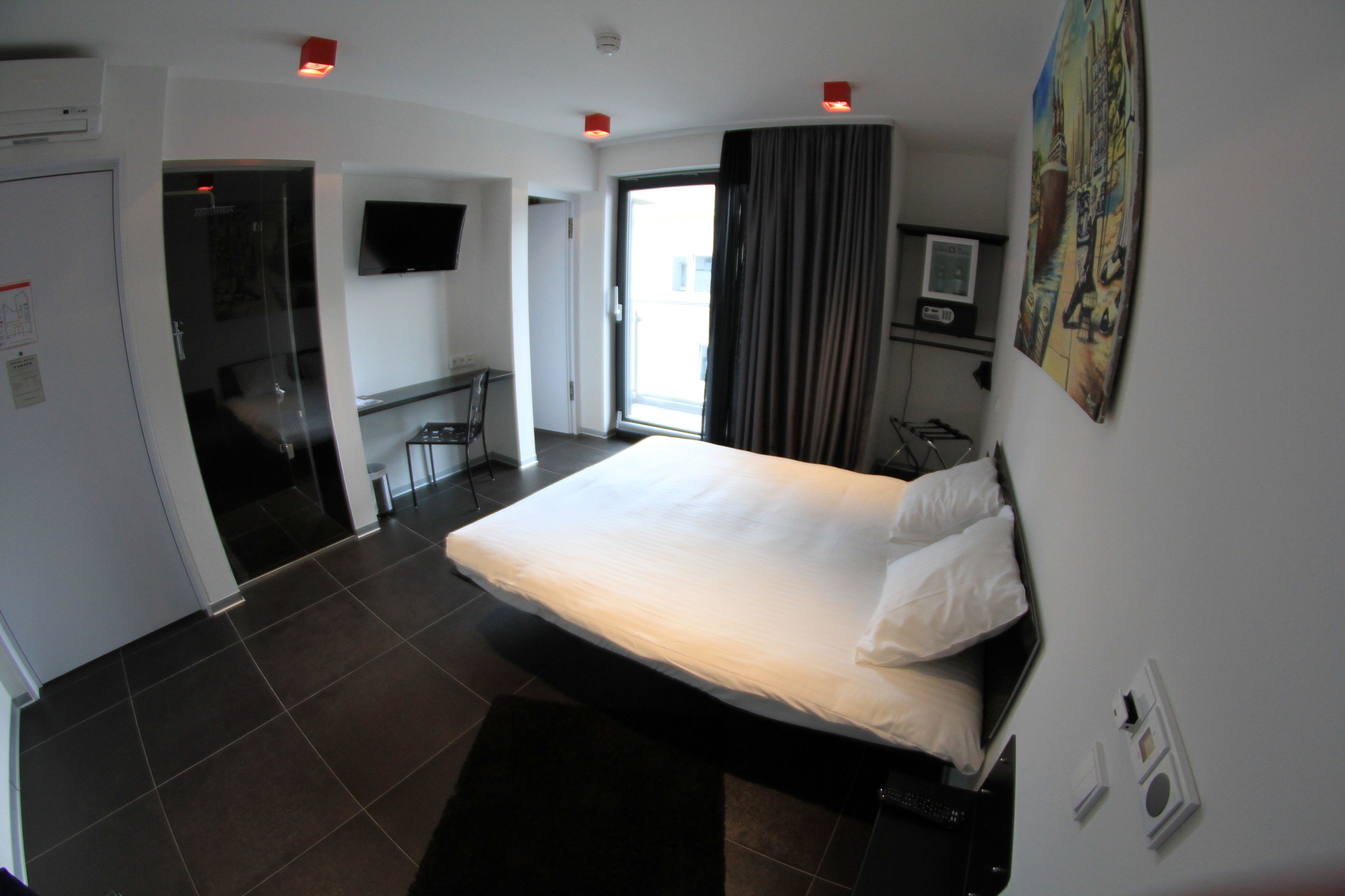 Quarto de hotel com cama, escrivaninha, cadeira, televisão e janela com cortinas.