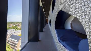 Corredor com vista para edifícios, parede estampada e um banco azul.