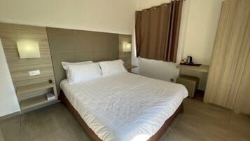 Quarto de hotel moderno com uma cama grande, cabeceira de madeira, mesa de cabeceira e pequena escrivaninha com cadeira.