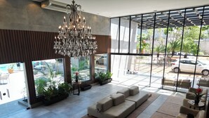 Um lobby moderno com um candelabro, área de estar e grandes janelas com vista para a rua.