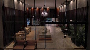 Um lobby moderno com área de estar, um candelabro e vista do espaço interior através de grandes portas de vidro.