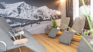 Uma área de spa com cadeiras reclináveis, um mural na parede de uma montanha nevada e uma pequena mesa com uma vela.