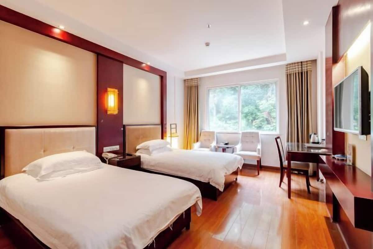 Quarto de hotel com duas camas, uma mesa, uma cadeira, televisão e janela com cortinas.