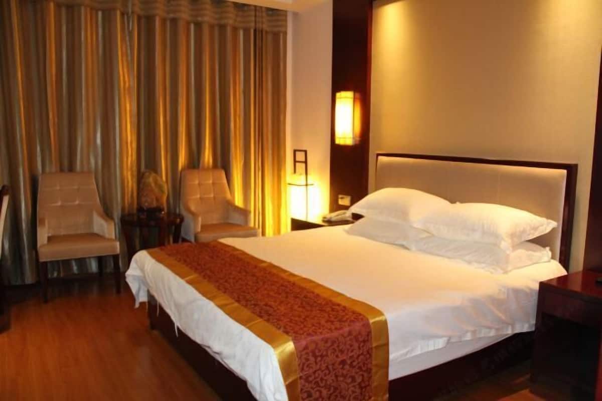 Quarto de hotel com uma cama grande, duas poltronas, uma mesa de cabeceira e um abajur.