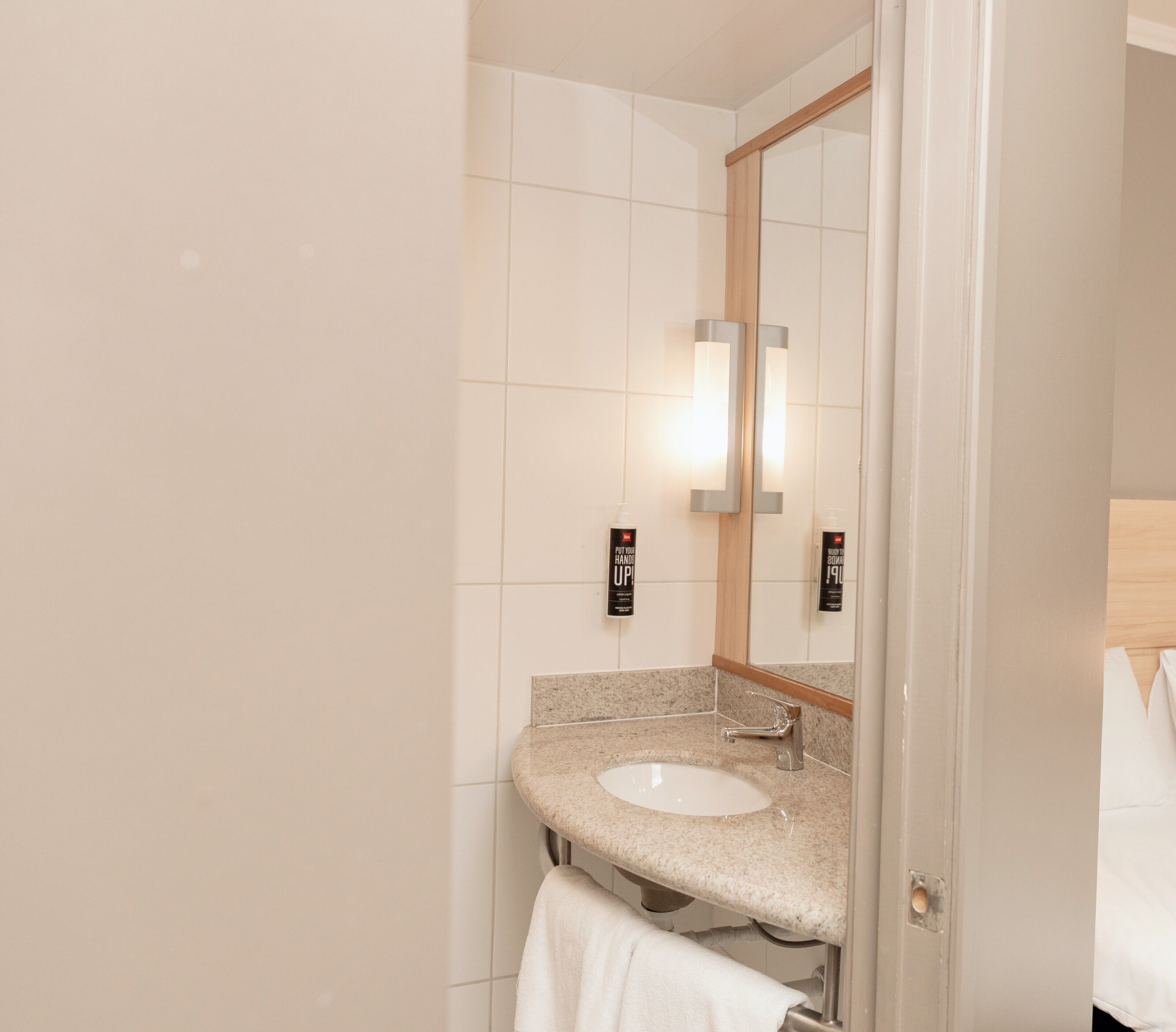 Casa de banho com lavatório branco, espelho e dois dispensadores de gel desinfetante.
