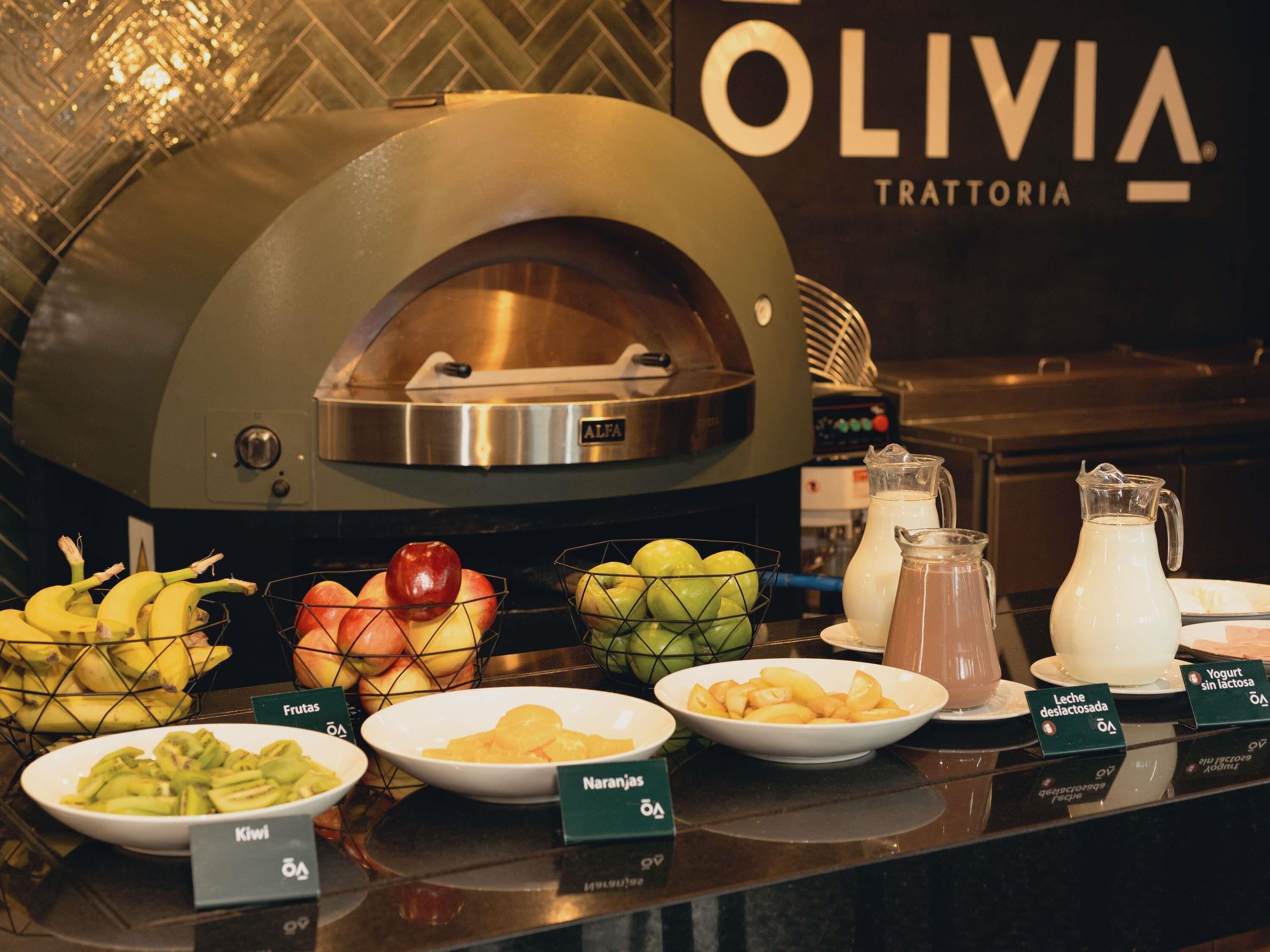 Uma estação de alimentos com forno a pizza, diversas frutas e recipientes identificados com kiwi e maçãs.