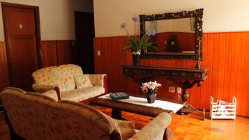Uma sala de estar com sofás de padrão floral, uma mesa de centro de madeira, um espelho e um vaso de planta.