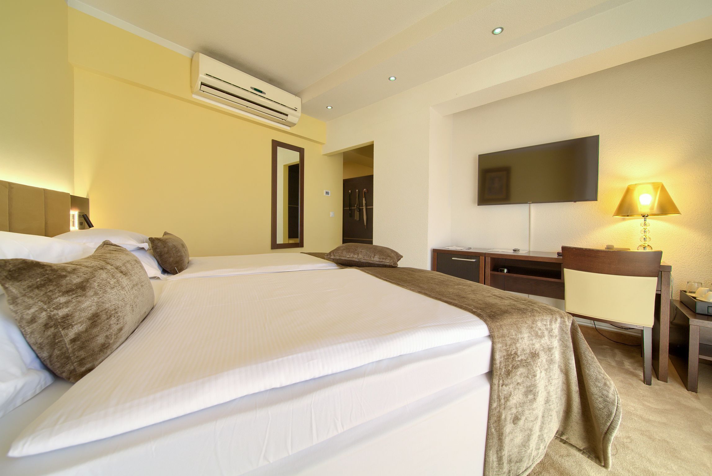 Quarto de hotel com cama, escrivaninha, televisão e ar condicionado.