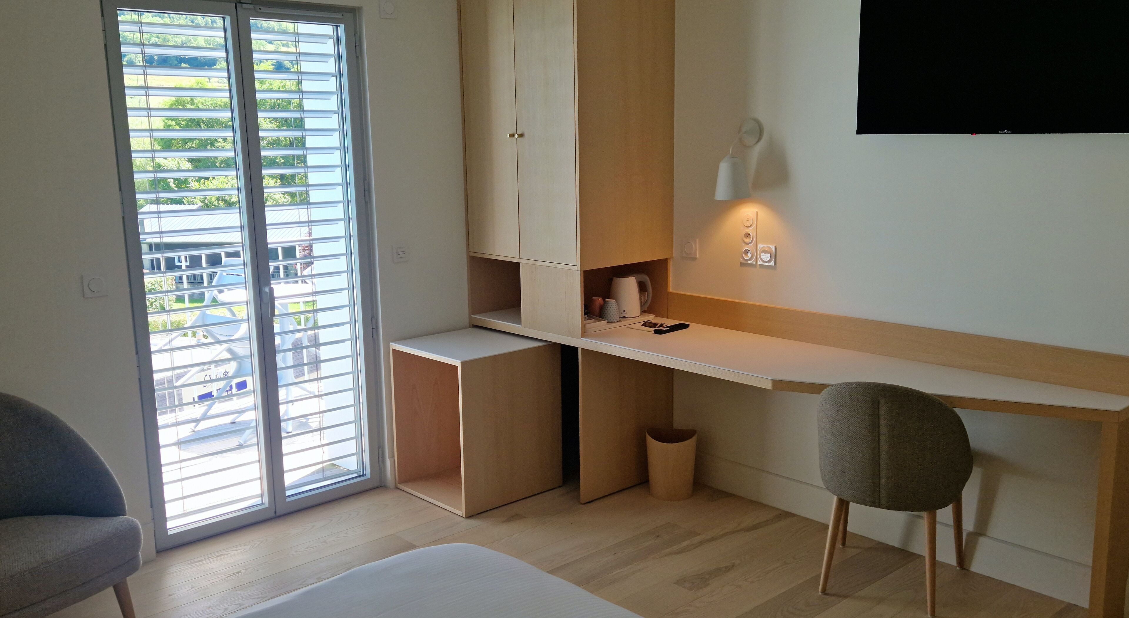 Quarto moderno com porta de vidro deslizante para uma varanda, uma escrivaninha de madeira, uma cadeira e uma cama.