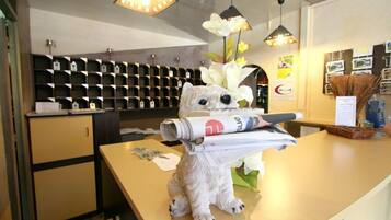 Balcão de recepção com escultura decorativa de um urso segurando um jornal. Atrás do balcão, existem prateleiras com garrafas e uma parede com quadros.