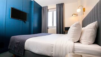 Quarto de hotel com cama, televisão de tela plana na parede, janela com cortinas e abajur.