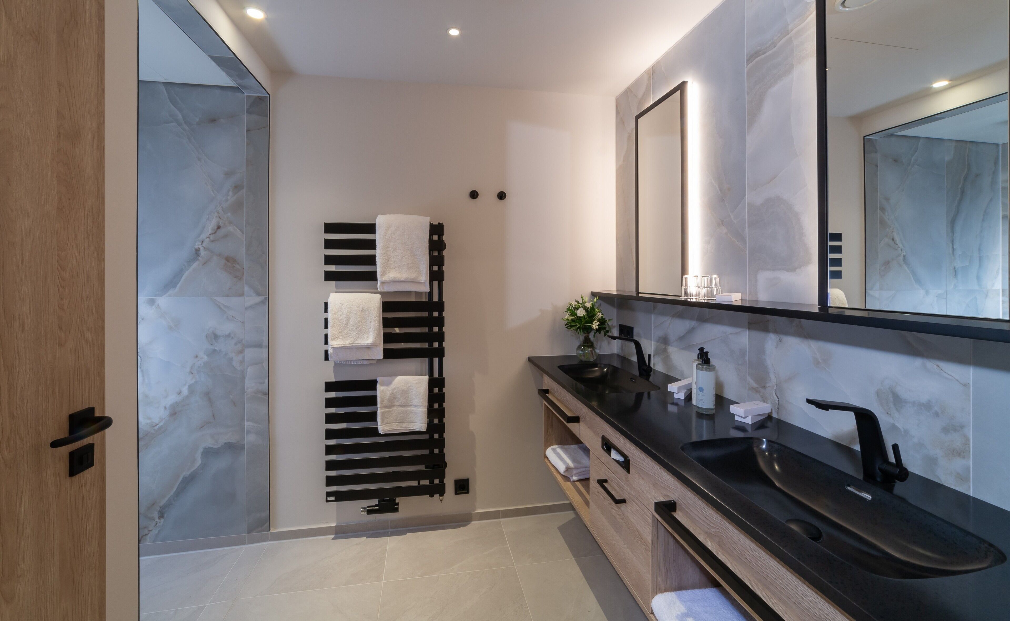 Uma casa de banho moderna com lavatório preto, um espelho grande e um porta-toalhas com vários toalhetes.