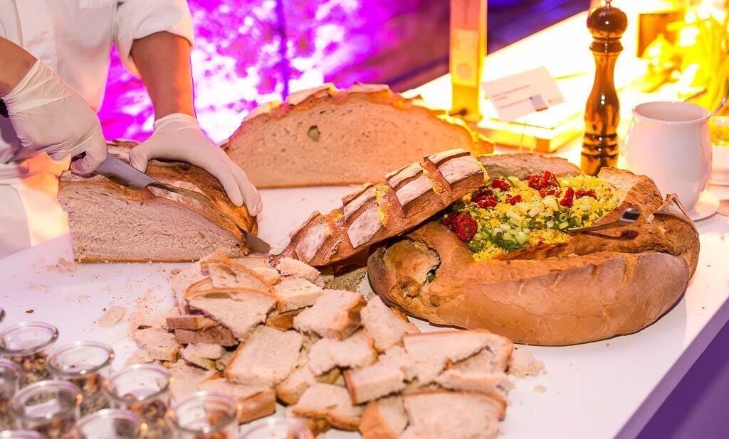 Uma mesa de buffet com diversos alimentos, incluindo pão fatiado e um prato empanado com cobertura.