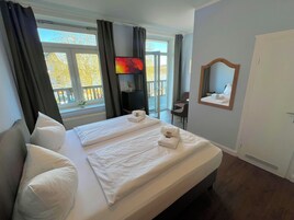 Quarto de hotel com cama grande, televisão, espelho e varanda com vista.