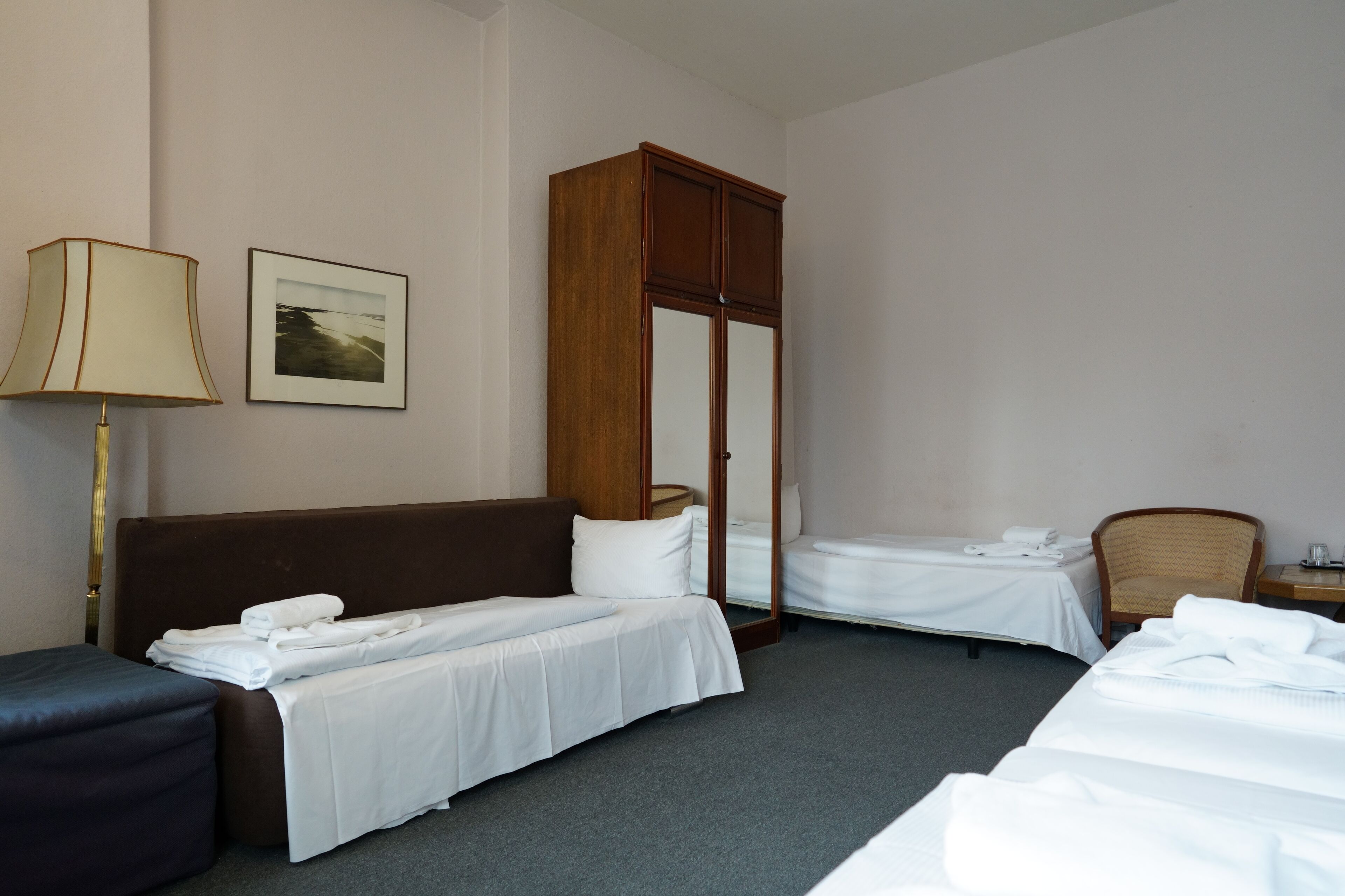 Quarto de hotel com duas camas, um sofá, uma poltrona, um abajur e um guarda-roupa.
