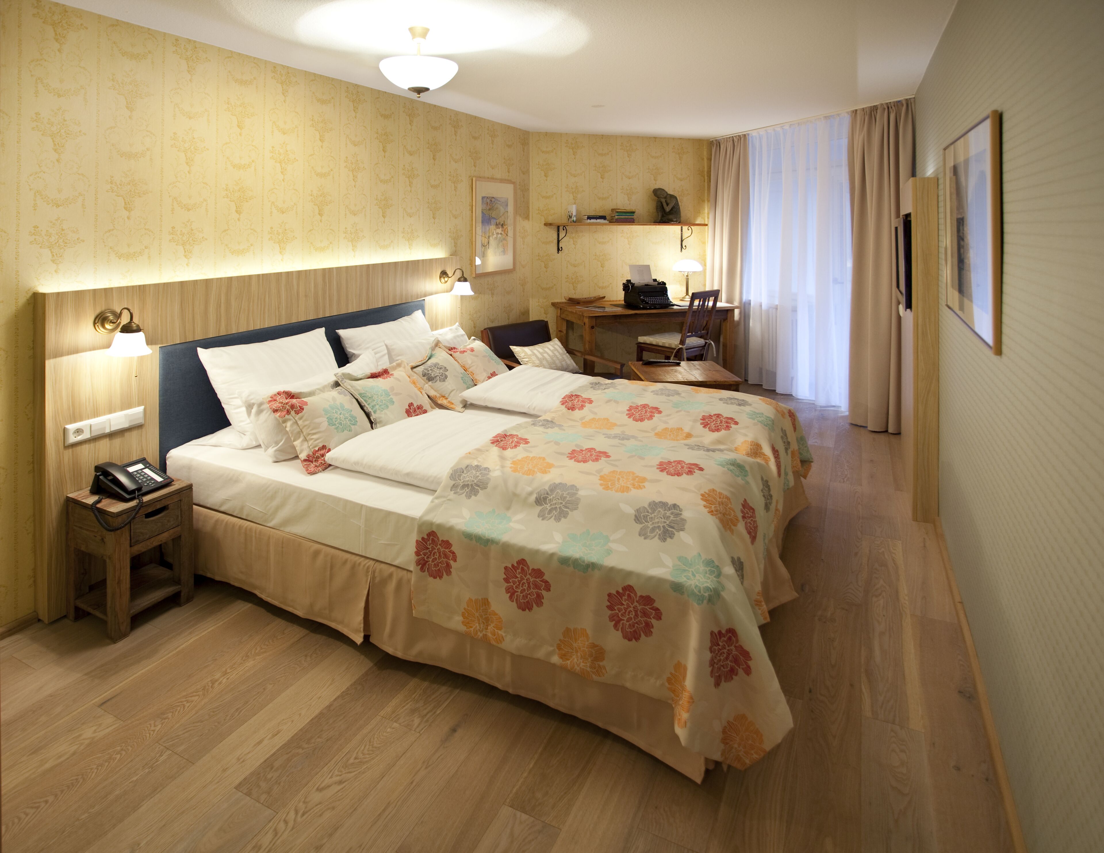 Quarto de hotel com uma cama grande, mesas de cabeceira, escrivaninha e uma cadeira.