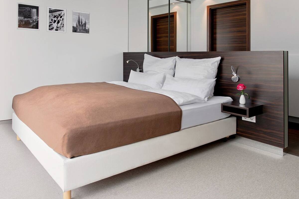 Quarto moderno com cama grande, mesa de cabeceira, espelho e criado-mudo com um vaso de flores.
