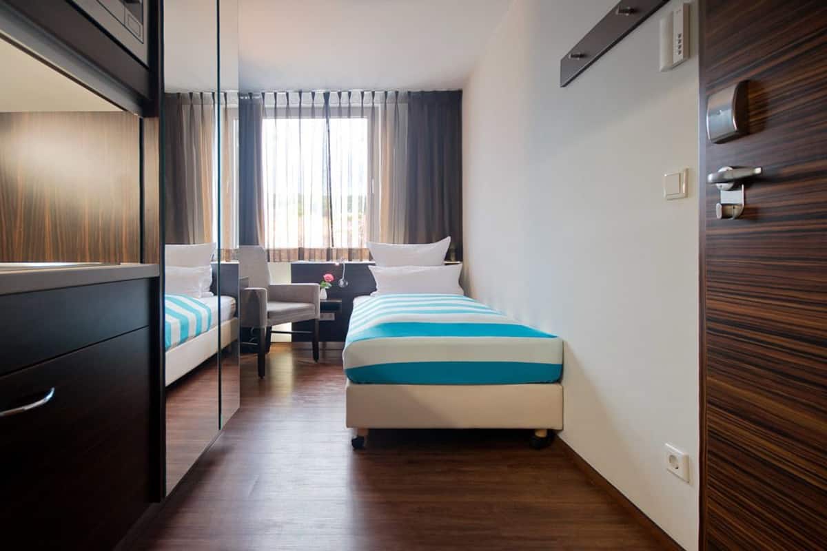 Quarto de hotel compacto com cama, escrivaninha e cadeira.