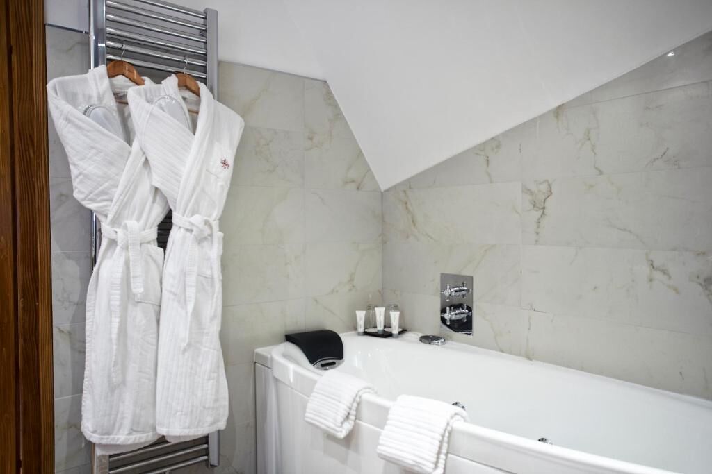 Um banheiro moderno com parede de mármore, uma banheira e dois roupões brancos pendurados em um porta-toalhas.