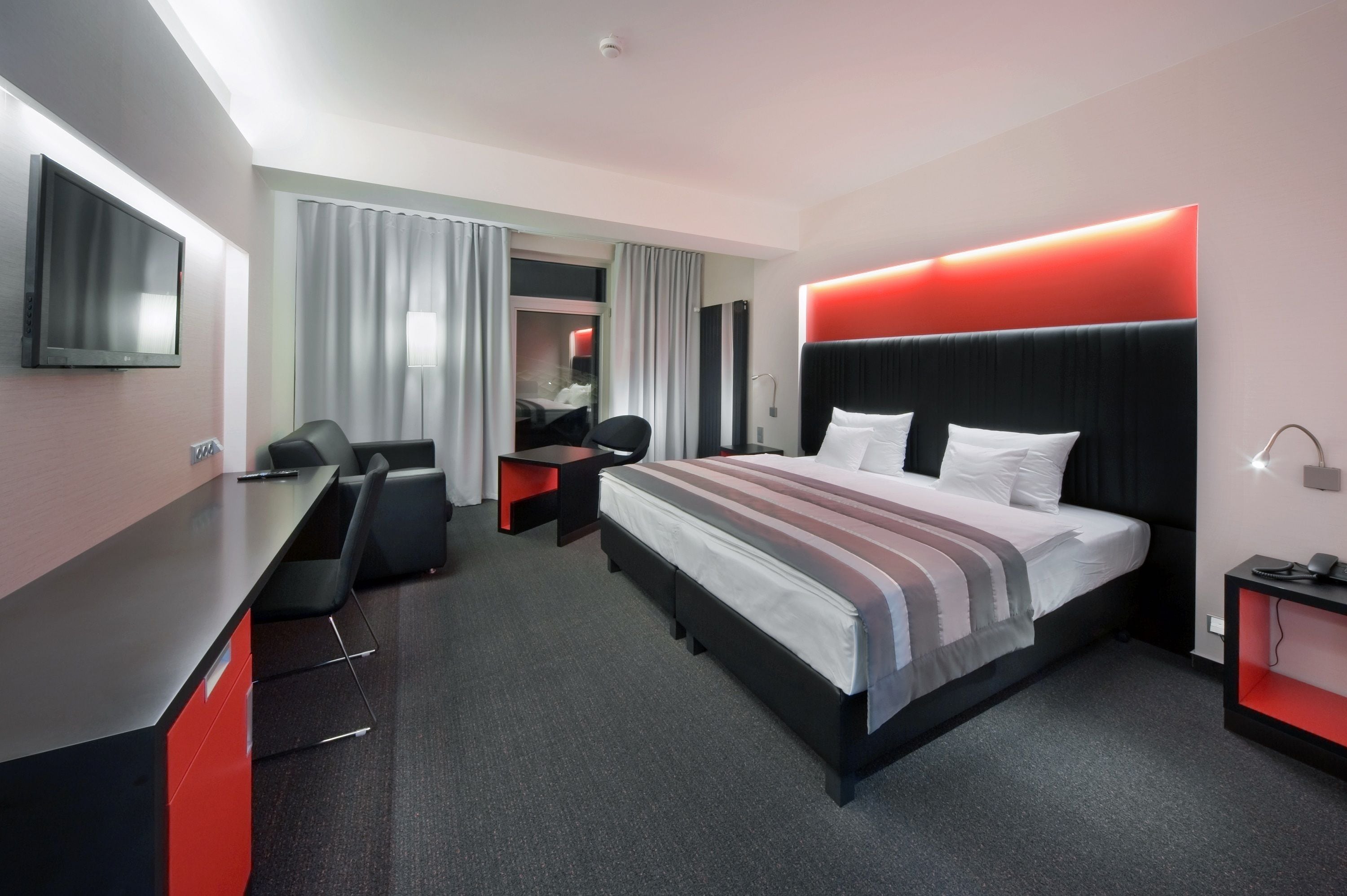 Quarto de hotel moderno com uma cama grande, uma escrivaninha, uma cadeira e uma televisão.