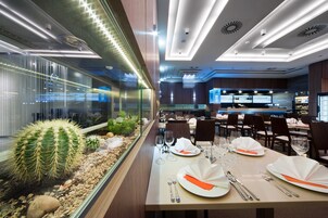Um restaurante com decoração moderna, apresentando uma exposição de cactos, mesas bem arrumadas e um espaço de bar.