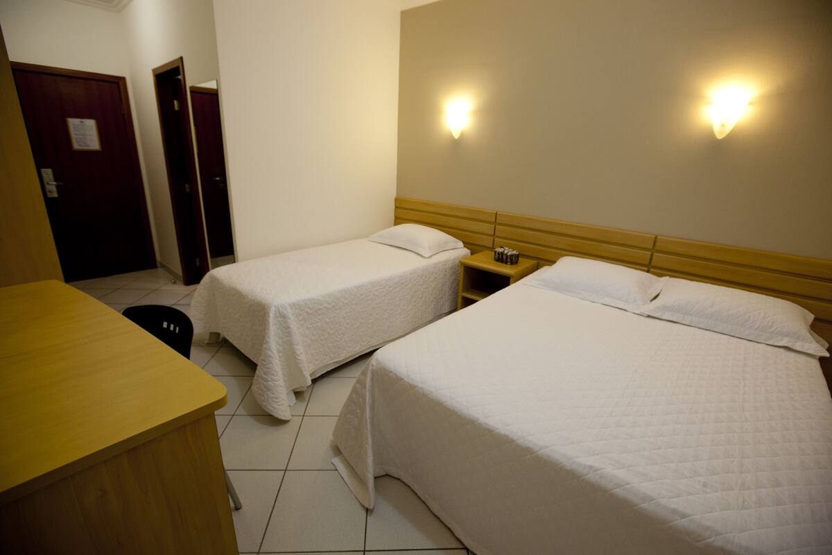 Quarto de hotel com duas camas de solteiro, uma escrivaninha de madeira e uma pequena mesa.