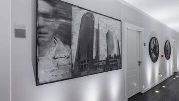 Um corredor com uma grande fotografia em preto e branco de edifícios na parede, uma porta e uma obra de arte circular na parede.