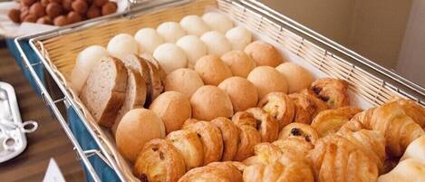 Exposição de diversos produtos de panificação, incluindo pão, croissants e pastéis redondos, provavelmente em uma padaria ou café.