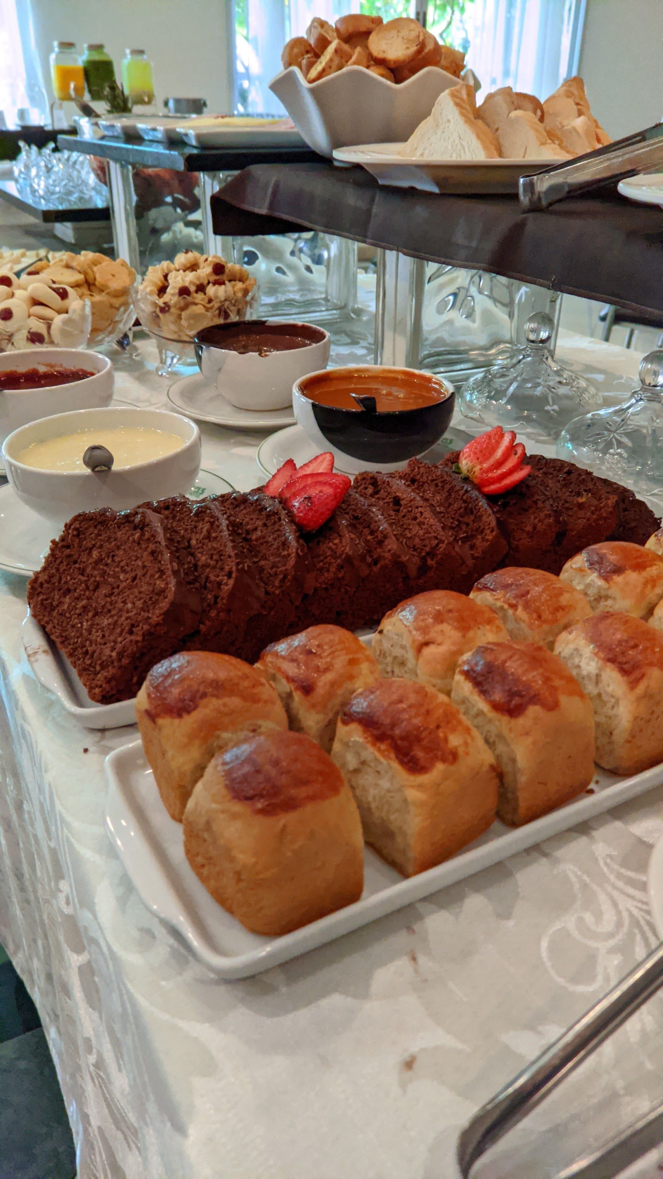 Buffet com diversos produtos de panificação, incluindo pães e um bolo de chocolate.
