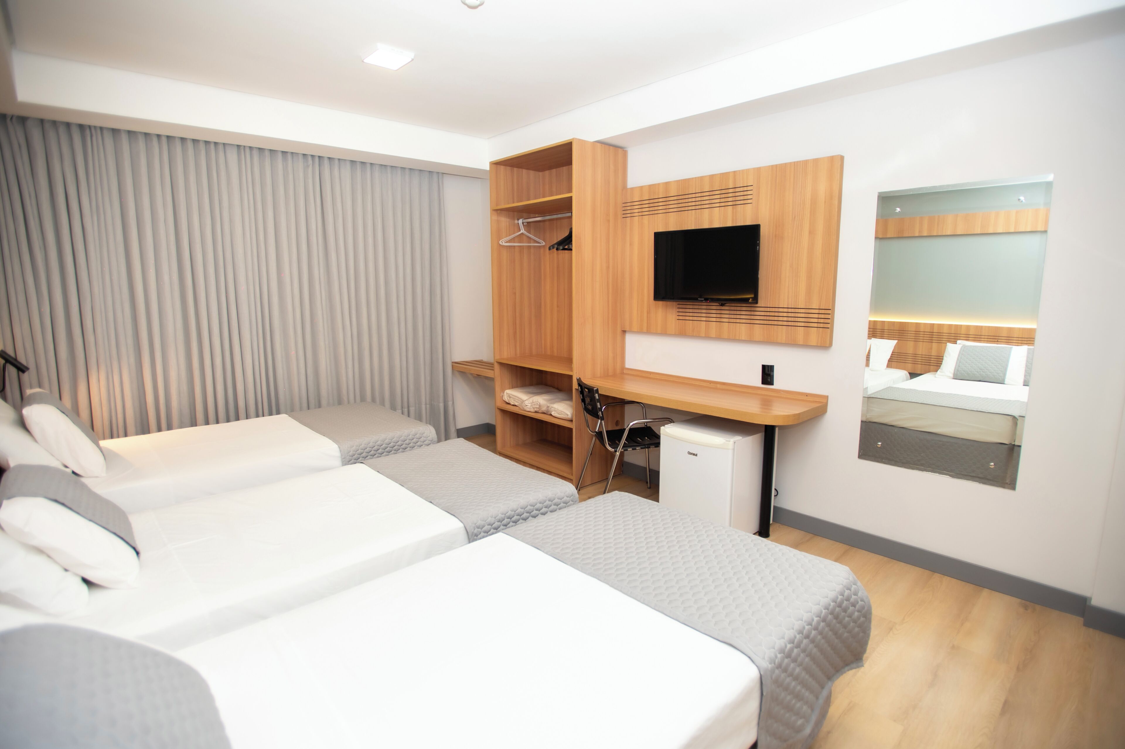 Quarto de hotel com duas camas, uma escrivaninha, uma televisão e um espelho.