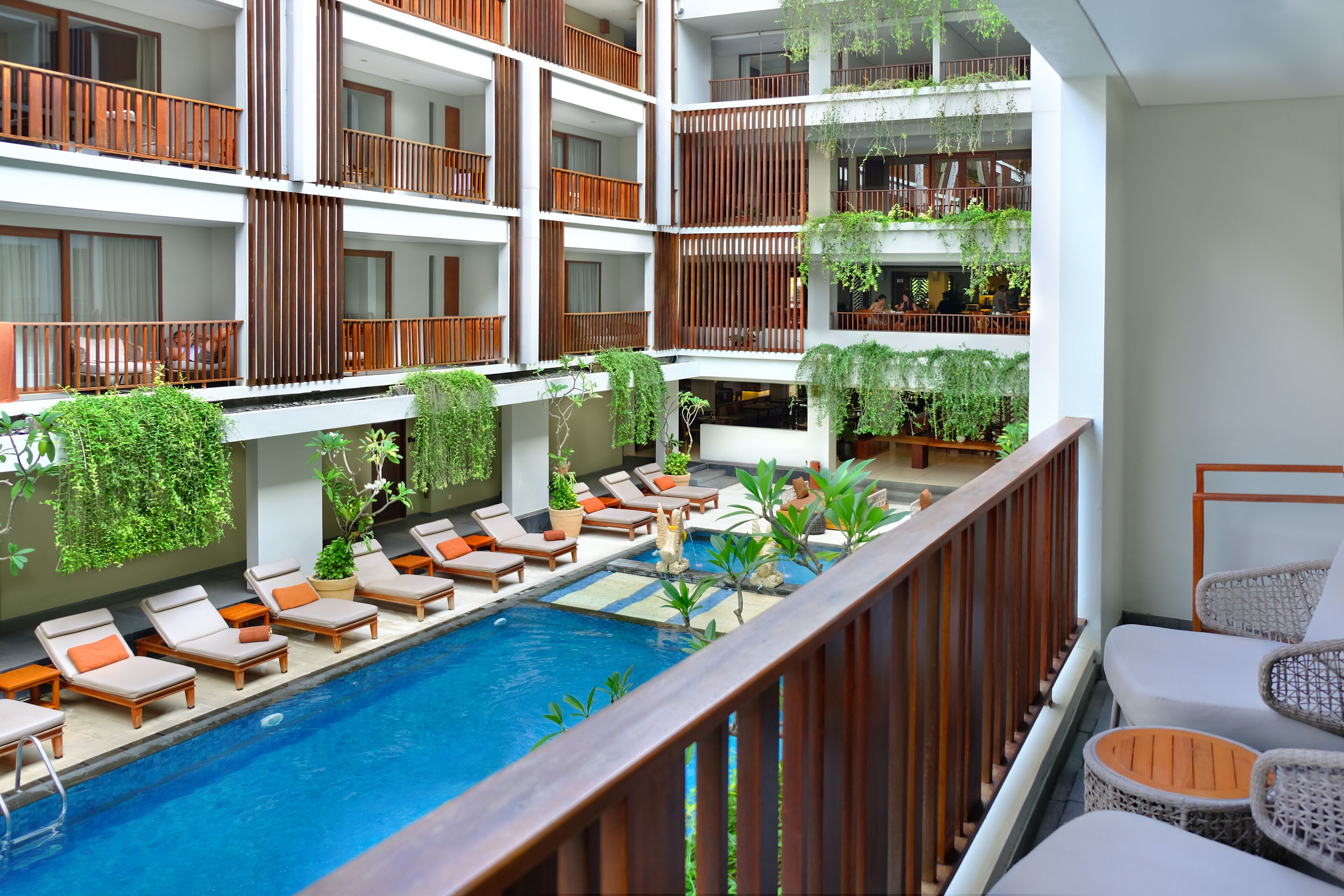 Um hotel com vários andares, piscina, espreguiçadeiras e jardins verticais.