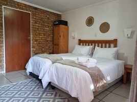 Quarto com parede de tijolos, cabeceira de madeira, cama com roupa de cama branca, mesa de cabeceira e tapete estampado.